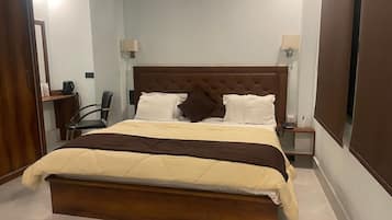 Quarto com cama grande, mesas de cabeceira, uma cadeira e uma escrivaninha.