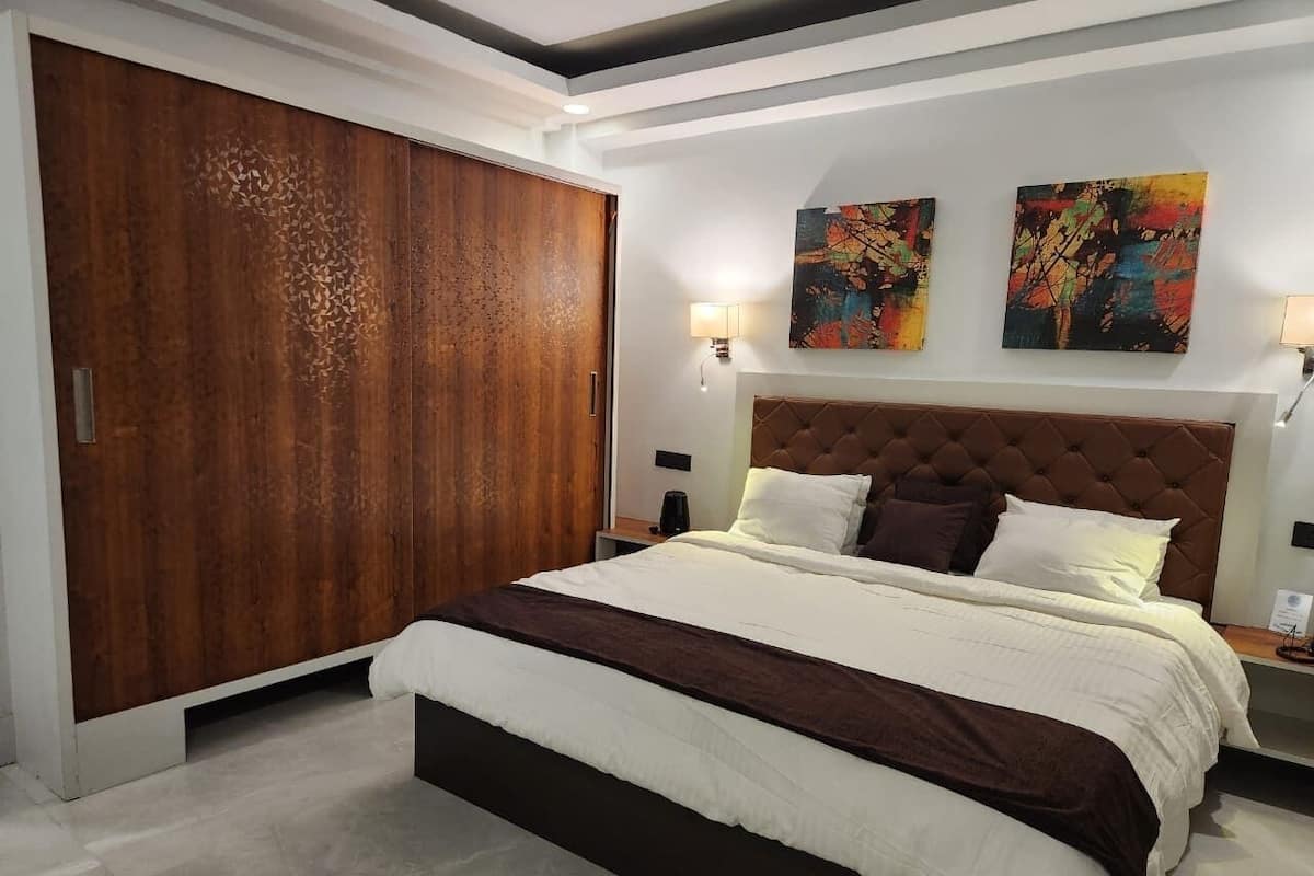Quarto moderno com uma cama grande, guarda-roupa de madeira e duas pinturas abstratas na parede.