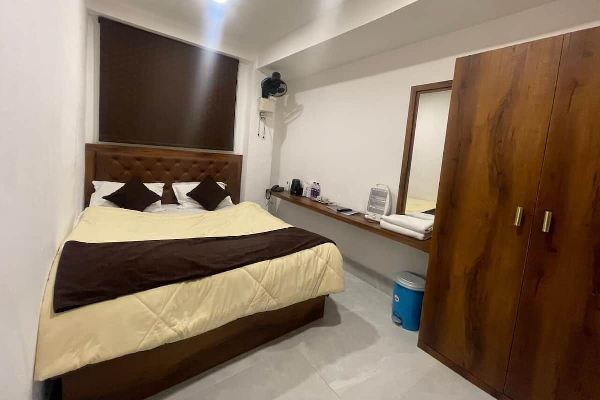 Quarto com cama, guarda-roupa, prateleira com produtos de higiene pessoal e uma pequena lixeira.