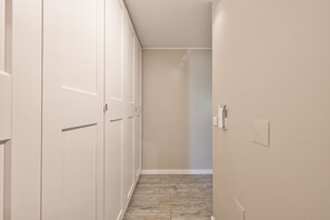 Um corredor estreito com portas brancas, chão de madeira e um interruptor de luz na parede.