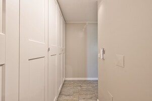 Um corredor estreito com portas brancas, chão de madeira e um interruptor de luz na parede.