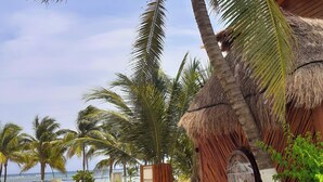 Um resort à beira-mar com palmeiras, um edifício com telhado de palha e vista para o oceano.