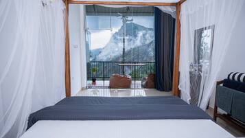 Quarto com uma cama grande, varanda com vista para uma montanha e área de estar com uma cadeira e almofadas.