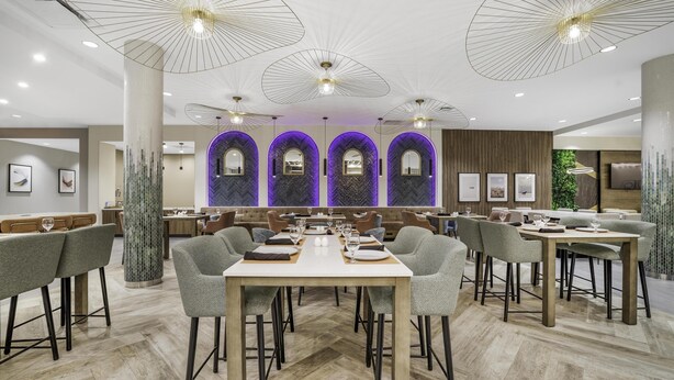Uma sala de jantar moderna com várias mesas e cadeiras, um pilar decorativo central e ventiladores de teto.
