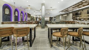 Um restaurante moderno com mesas e cadeiras altas, um pilar decorativo central e um bar com prateleiras cheias de garrafas.