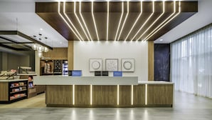 Uma área de recepção de hotel com design moderno, apresentando um balcão de atendimento, painel de parede em madeira e uma grande janela com vista.