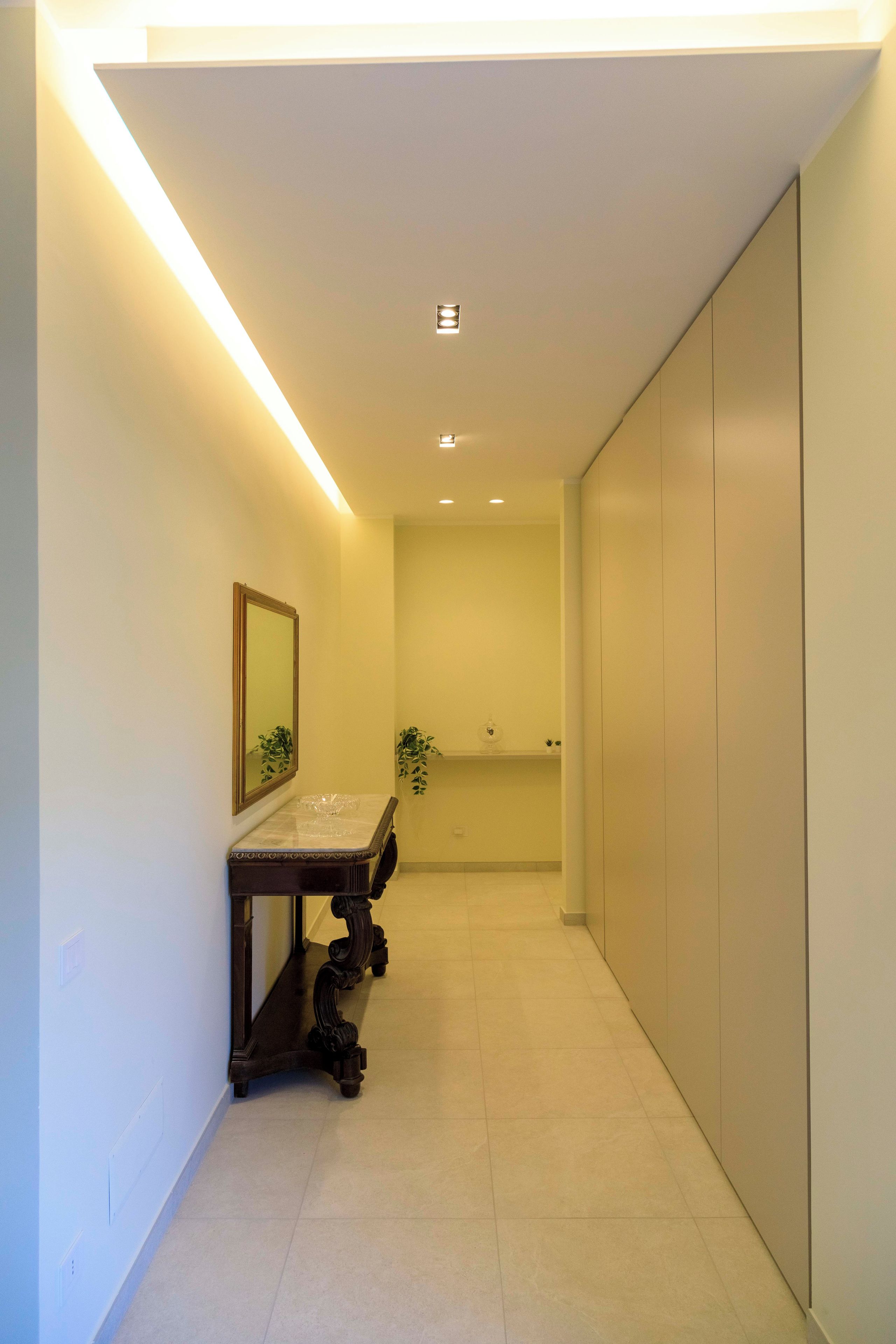 Um corredor com uma mesa de mármore, um espelho e uma planta.