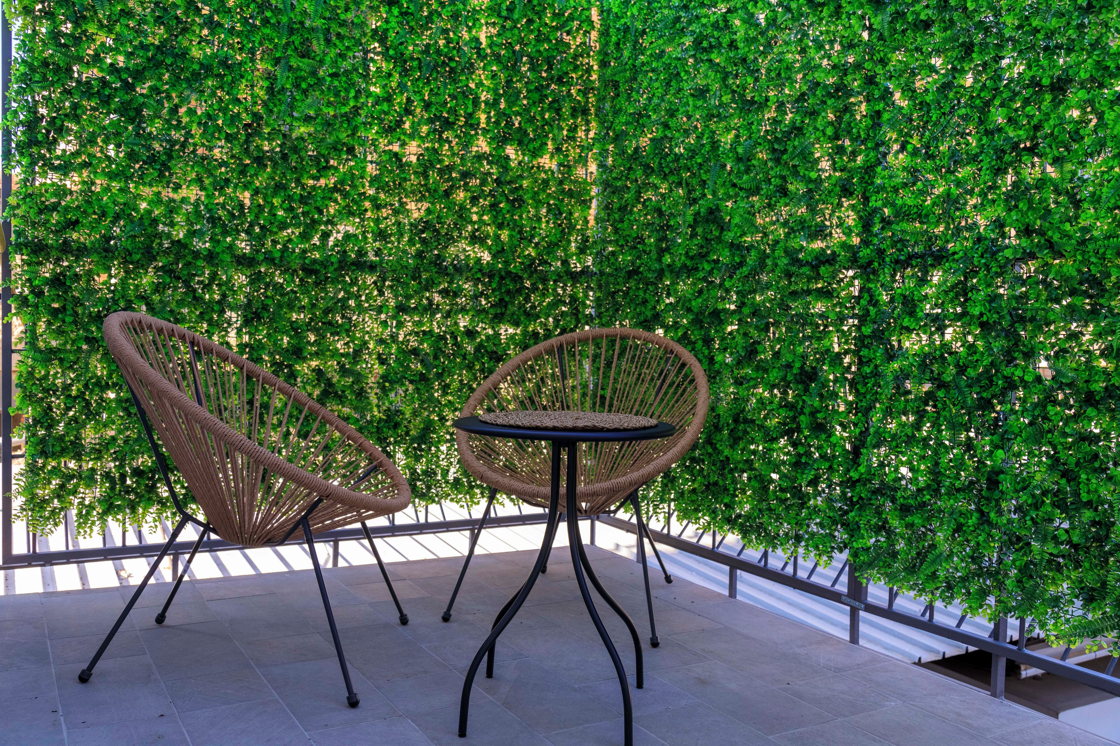 Um terraço com duas cadeiras de vime e uma mesa pequena, ladeado por um muro verde exuberante.