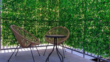 Um terraço com duas cadeiras de vime e uma mesa pequena, ladeado por um muro verde exuberante.