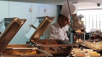 Disposição de buffet com diversos recipientes de comida e um cozinheiro de uniforme.