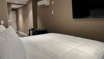 Quarto de hotel com cama, secretária, cadeira, ar condicionado, televisão e porta.