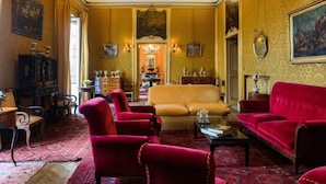 Um quarto com um sofá vermelho, um sofá amarelo e uma poltrona vermelha. Há um candelabro no centro do aposento.