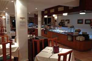Um restaurante com balcão de buffet, cadeiras e mesas de madeira preparadas para refeições.