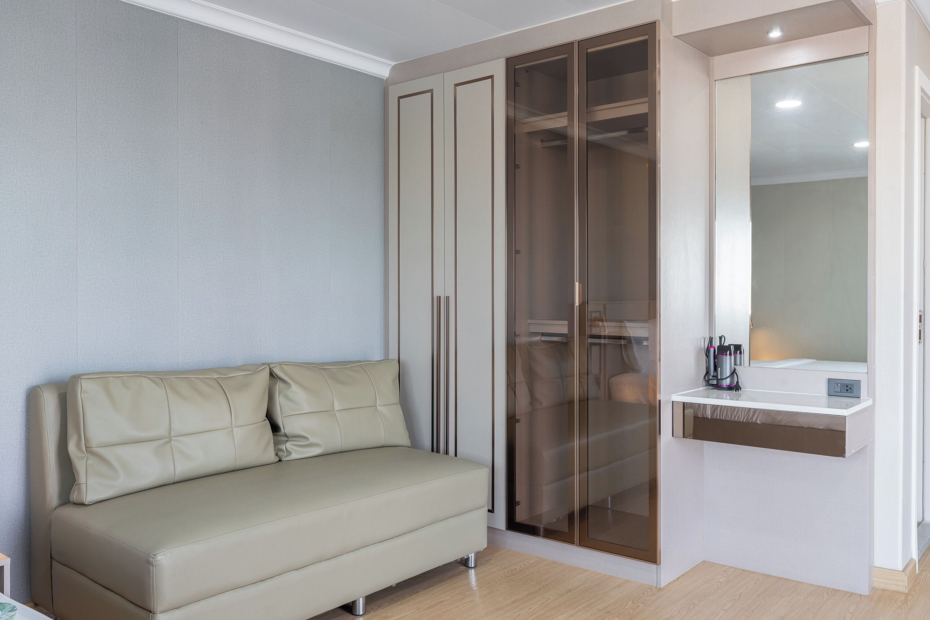 Quarto moderno com sofá bege, closet espaçoso e pequena toucador com espelho.
