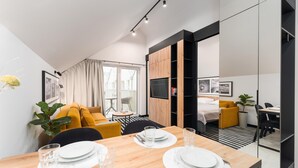 Quarto de hotel moderno com área de refeições, sofá, televisão e cama.