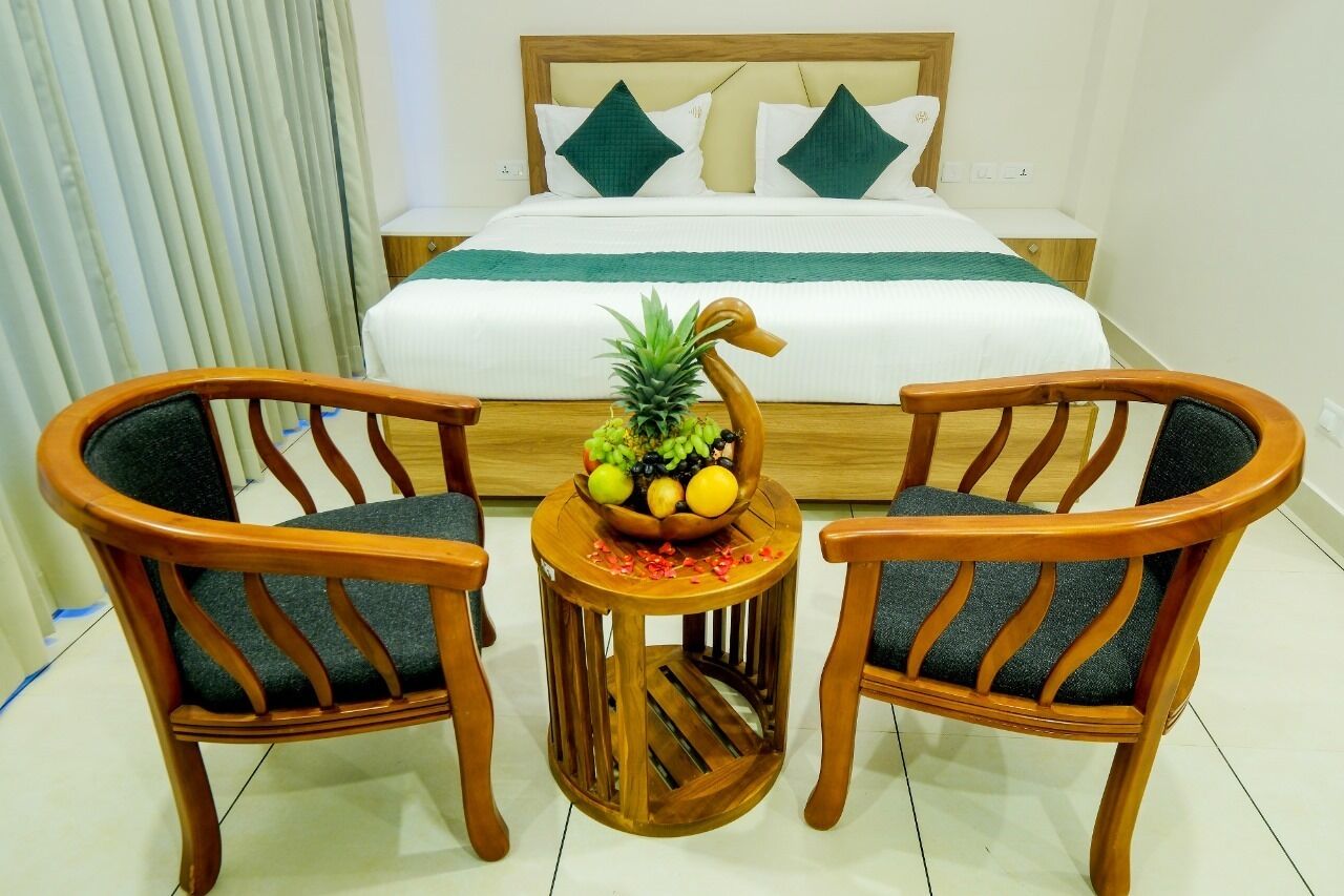 Quarto de hotel com uma cama, duas cadeiras de madeira e uma mesinha com uma fruteira.