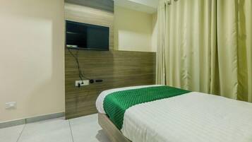 Quarto de hotel com uma cama, uma TV de tela plana presa a um painel de madeira e uma cortina na janela.