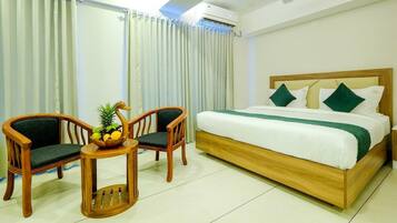 Quarto com cama de madeira, duas cadeiras de madeira, uma mesinha redonda com uma tigela de frutas e uma janela com cortinas.