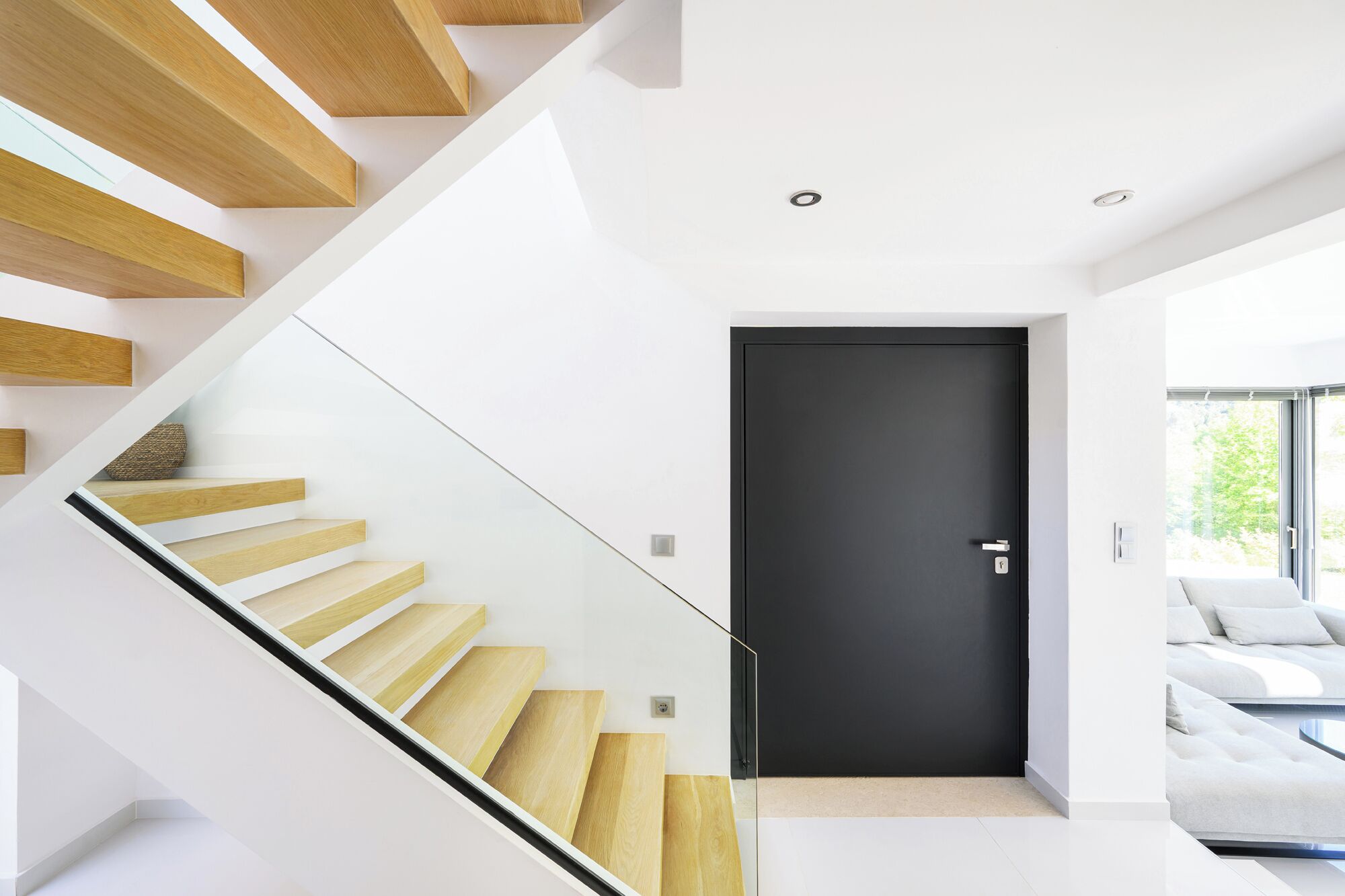 Um interior moderno com uma escada que leva a uma porta escura, um guarda-corpo de vidro e um sofá branco.