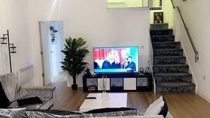 Uma sala de estar moderna com uma televisão de tela plana, uma escada e um vaso de planta.