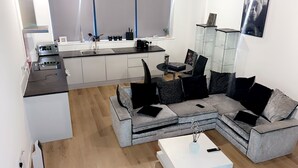 Uma sala de estar moderna com um sofá modular cinzento, uma mesa de centro branca e uma área de cozinha com pia e bancada.