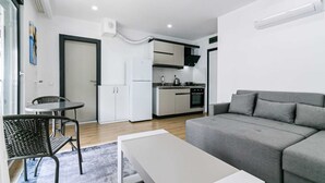 Um apartamento moderno com cozinha compacta, um sofá cinza, uma mesa de jantar com cadeiras e uma mesa de centro branca.