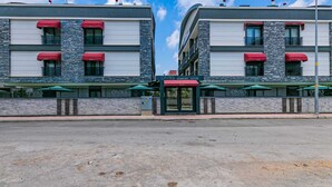 Hotel com fachada moderna, apresentando elementos de pedra e vidro, e toldos vermelhos sobre as janelas.