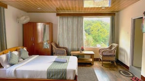 Quarto com cama, duas cadeiras de vime, guarda-roupa de madeira, uma mesinha e janela com cortinas.