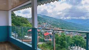 Varanda com vista para uma vila na encosta, corrimão e interior parcialmente visível com teto.