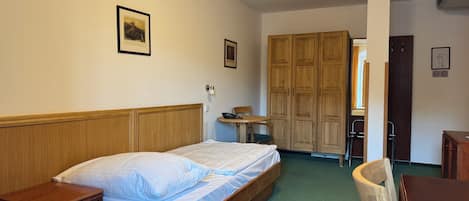 Quarto de hotel com cama de madeira, uma escrivaninha, uma cadeira e um guarda-roupa.