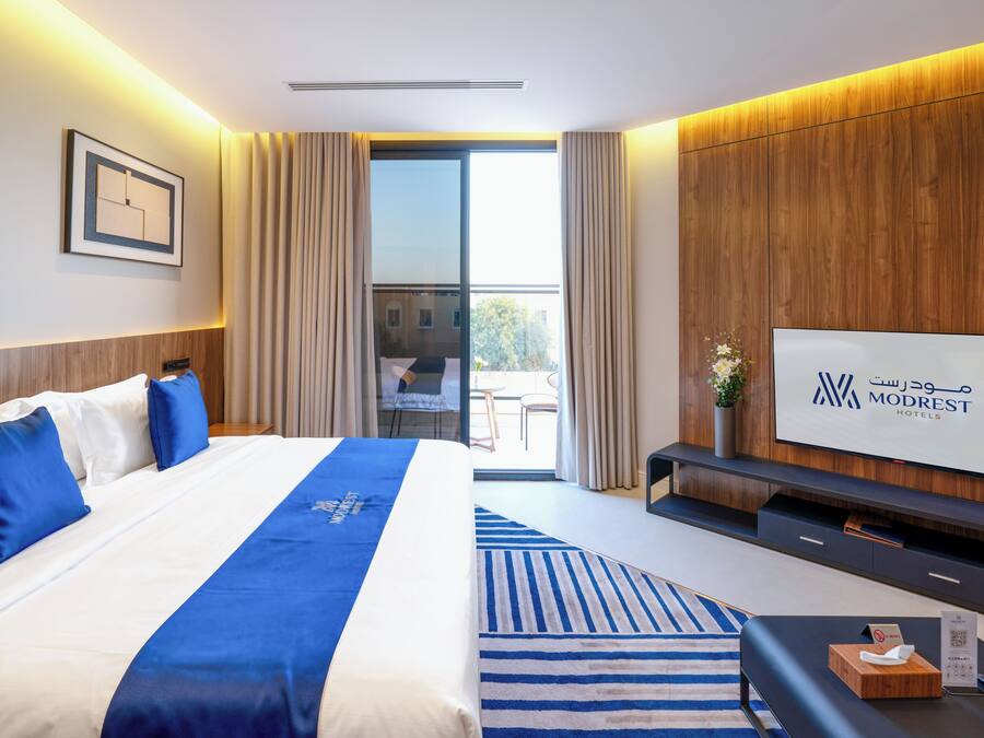 Quarto de hotel moderno com uma cama grande, televisão de tela plana, parede de destaque em madeira e vista para o exterior.