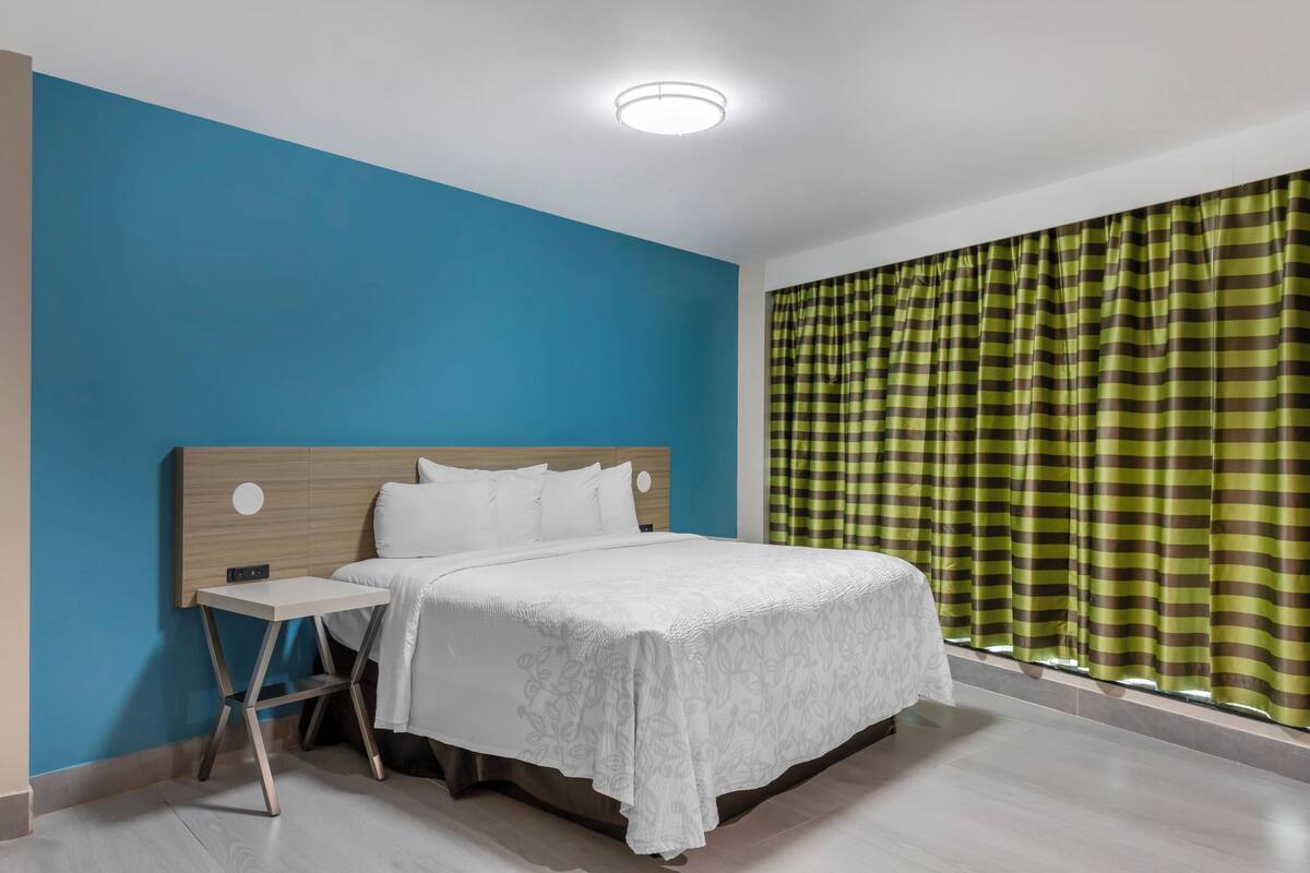 Quarto com cama, mesa de cabeceira e janela com cortinas.