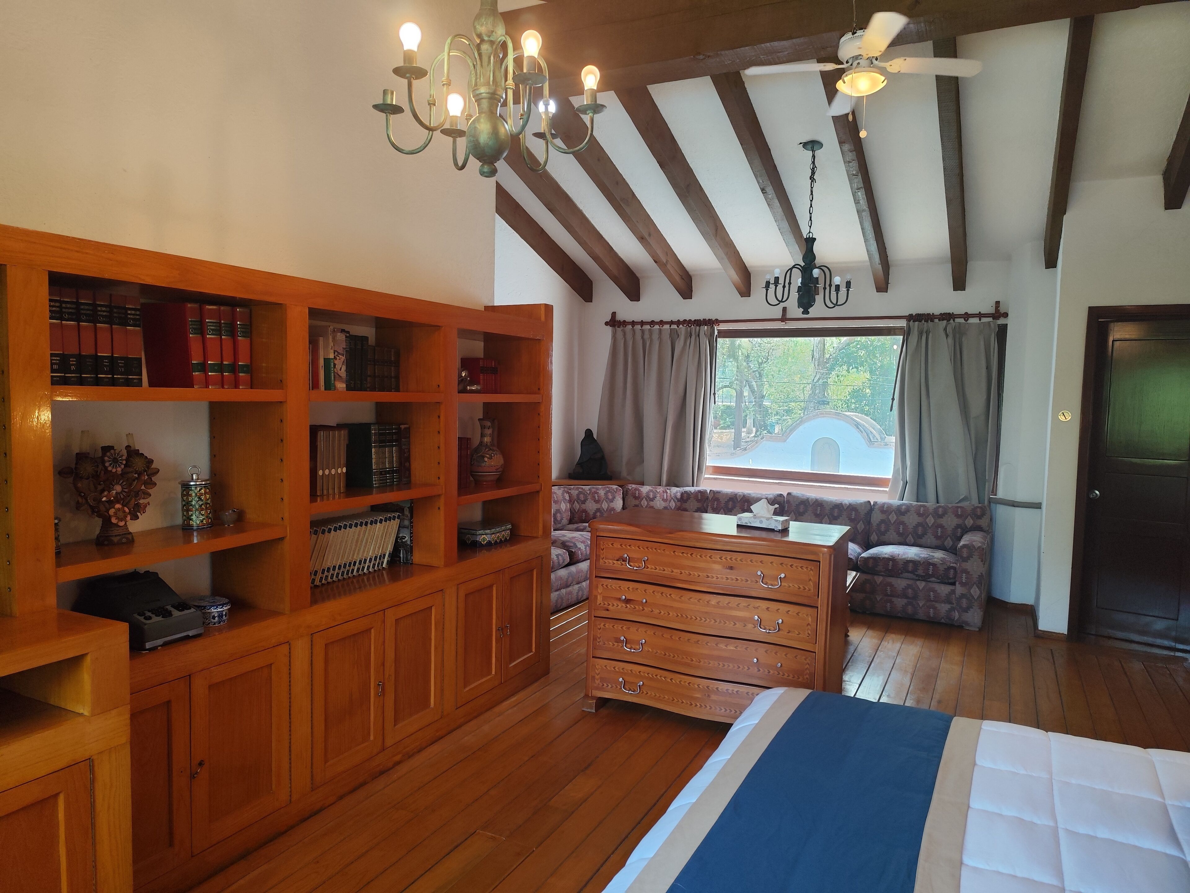 Um quarto acolhedor com estantes de madeira, um sofá estampado, um aparador de madeira e uma janela grande com cortinas.