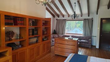 Um quarto acolhedor com estantes de madeira, um sofá estampado, um aparador de madeira e uma janela grande com cortinas.