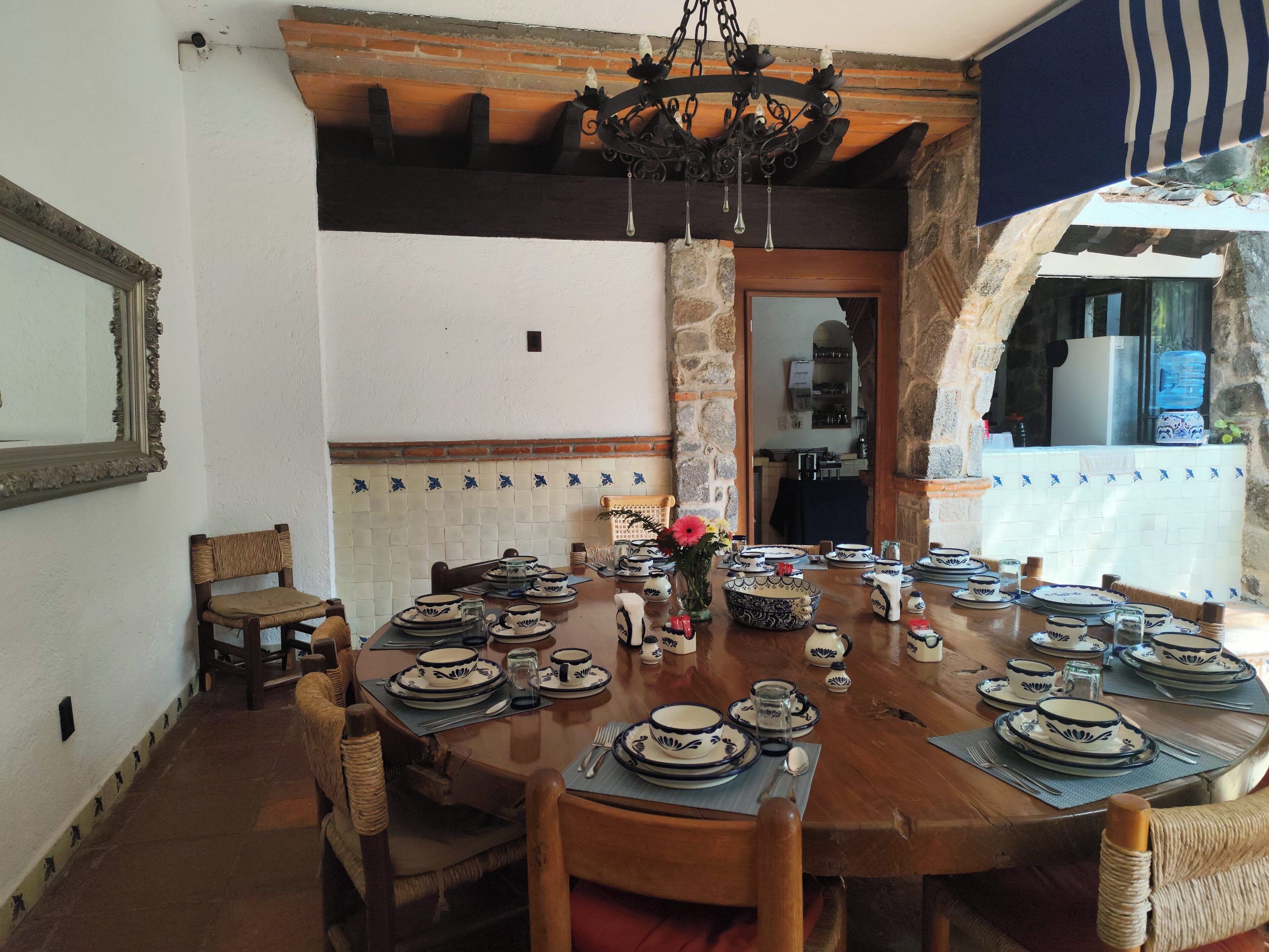 Uma sala de jantar com uma grande mesa de madeira posta para uma refeição, rodeada por cadeiras.