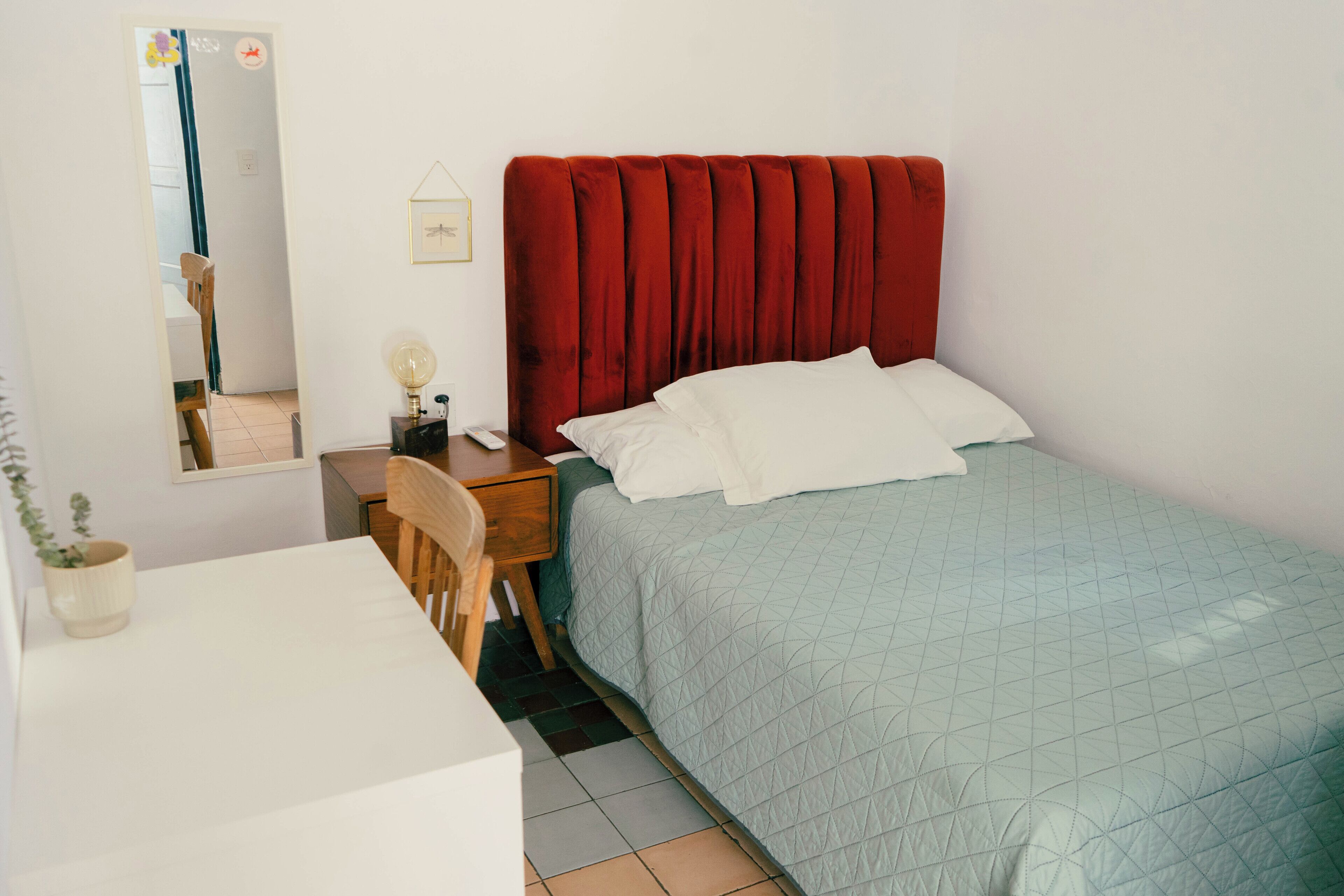Quarto com cama, escrivaninha, cadeira, espelho e uma pequena planta.