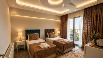 Quarto de hotel com duas camas, uma janela grande com cortinas, um radiador e um tapete estampado.