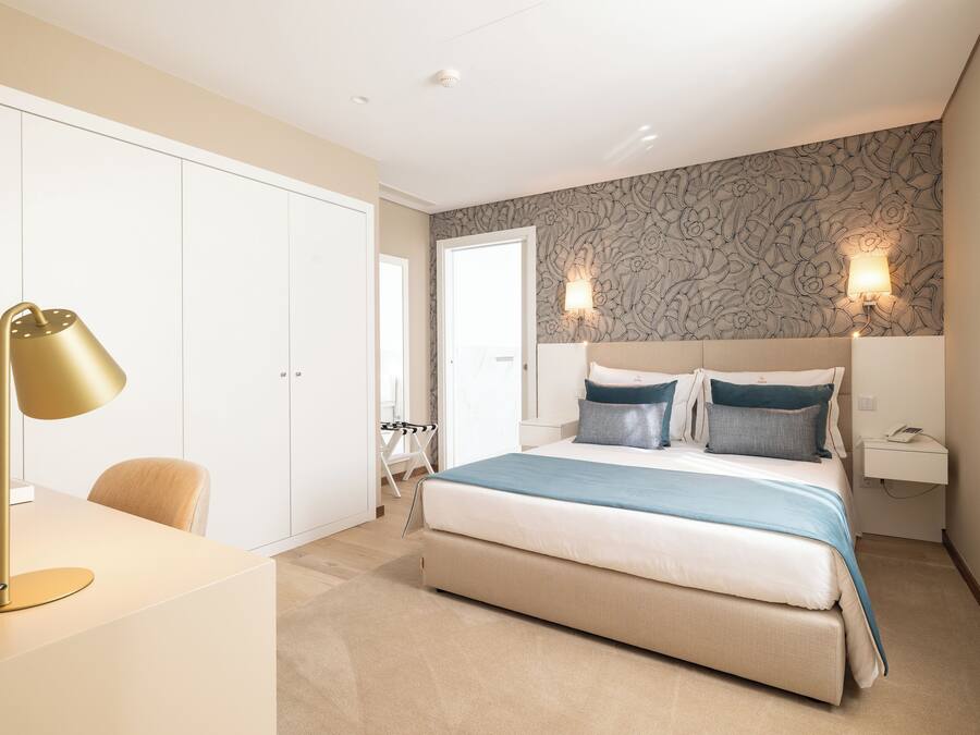 Quarto moderno com cama, mesas de cabeceira, escrivaninha e abajur.
