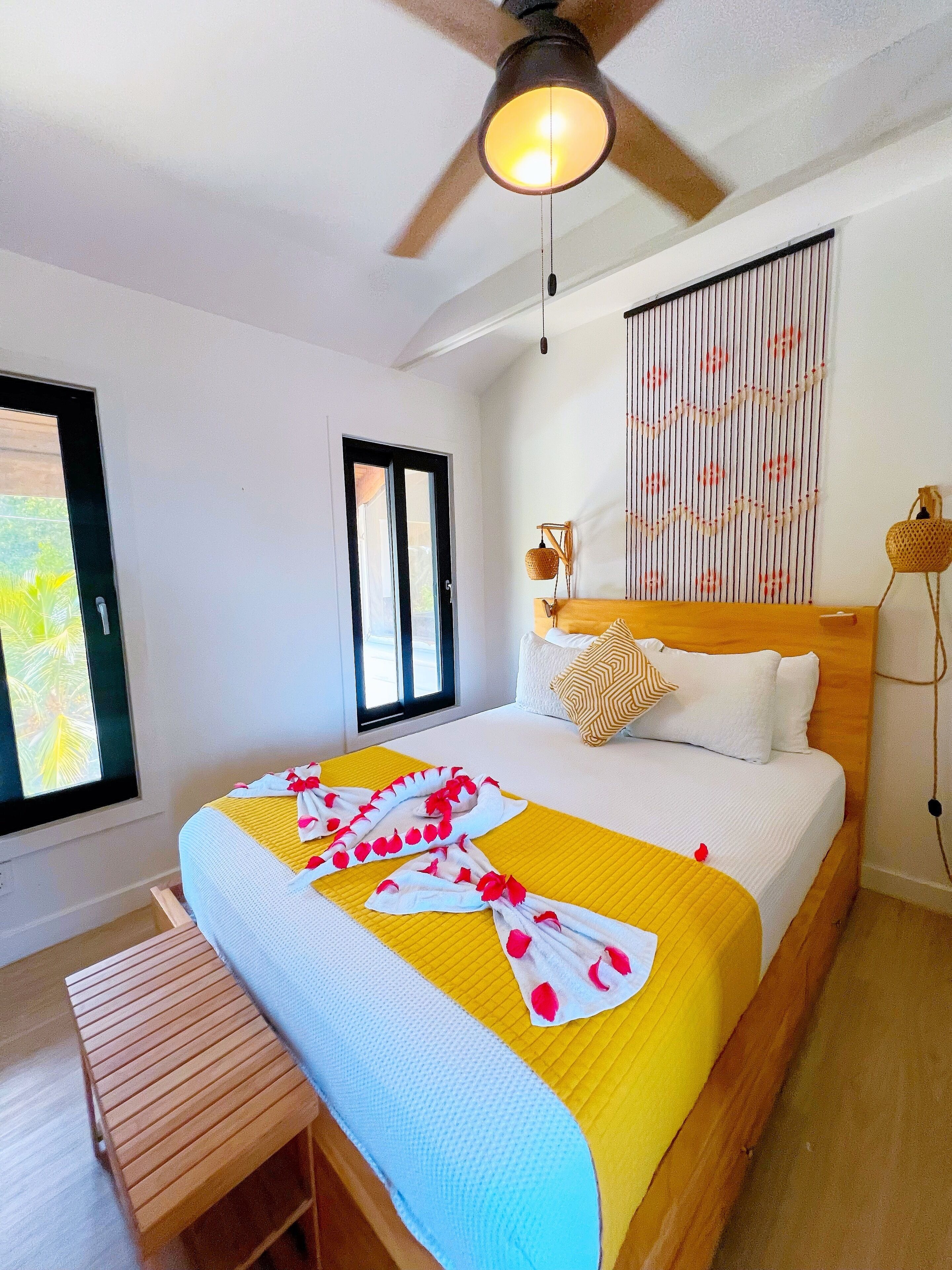 Quarto de hotel com cama, ventoinha no teto, janela e um adorno na parede.