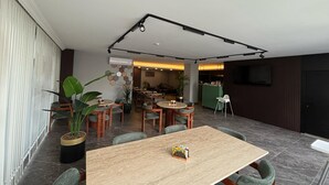 Uma área de refeições moderna com uma mesa central, rodeada por cadeiras, e um bar ao fundo.