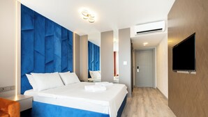Quarto de hotel moderno com uma cama grande, televisão de tela plana e piso de madeira.