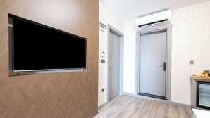 Um corredor moderno com televisão de tela plana fixada em parede de madeira, uma porta com puxador e um aparelho de ar condicionado na parede.