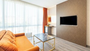 Uma sala de estar moderna com sofá, mesa de centro, televisão de tela plana na parede e área de cozinha com bancada e armários.