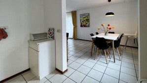 Uma cozinha moderna com armários brancos, um balcão pequeno e uma área de refeições com mesa branca e cadeiras pretas.