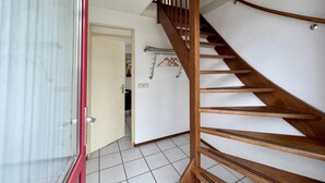 Uma escadaria com degraus de madeira e corrimão, que leva a um quarto com uma porta branca e uma pequena janela.