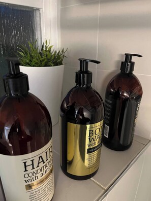 Três frascos de condicionador de cabelo com óleo de amêndoa numa prateleira de casa de banho.