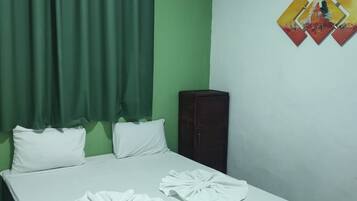 Quarto com uma cama, parede verde, ar condicionado, guarda-roupa escuro e uma obra de arte pendurada na parede.