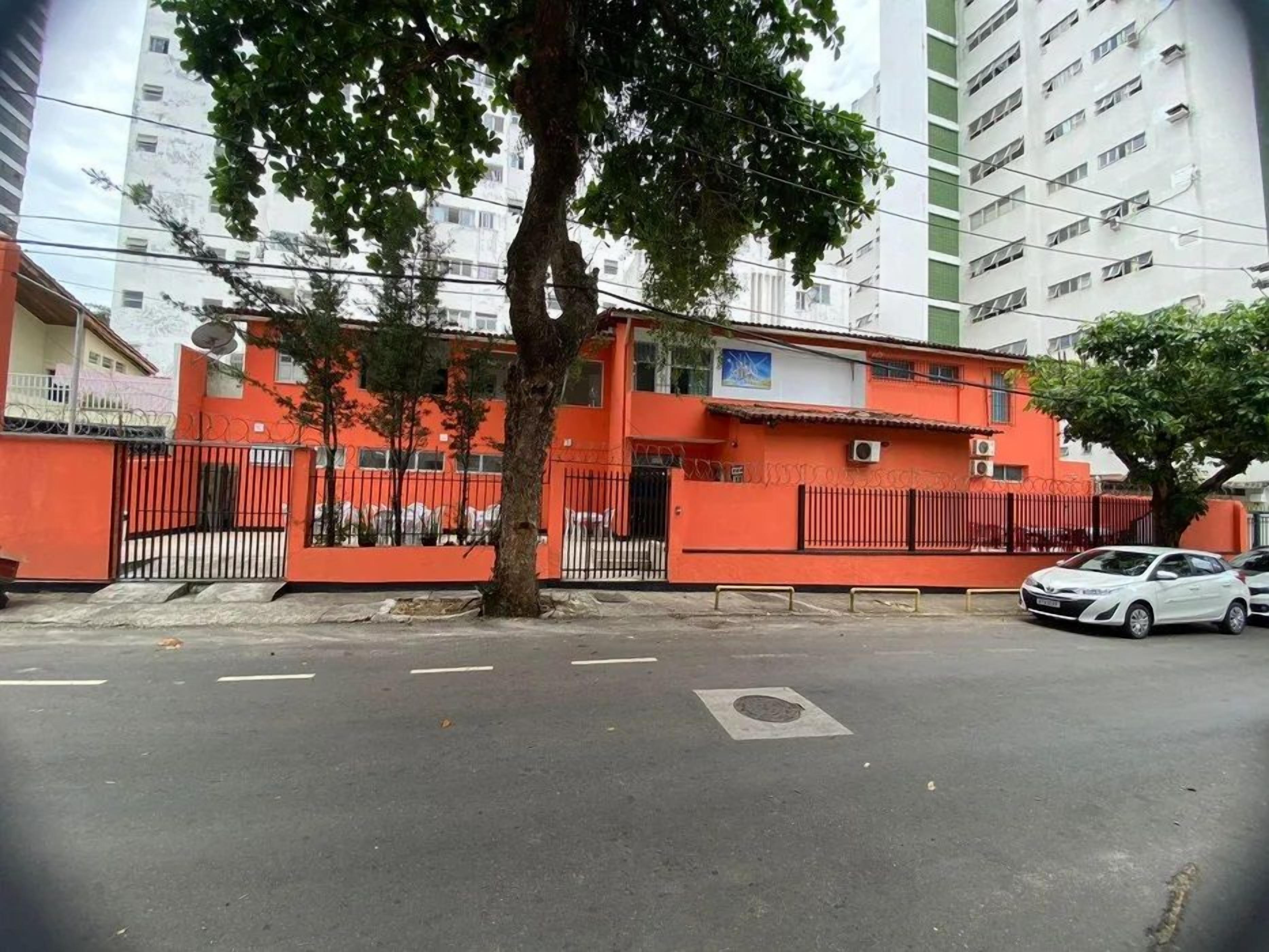 Um edifício com fachada vermelha, portão e uma árvore na frente.