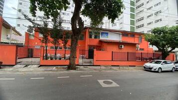 Um edifício com fachada vermelha, portão e uma árvore na frente.