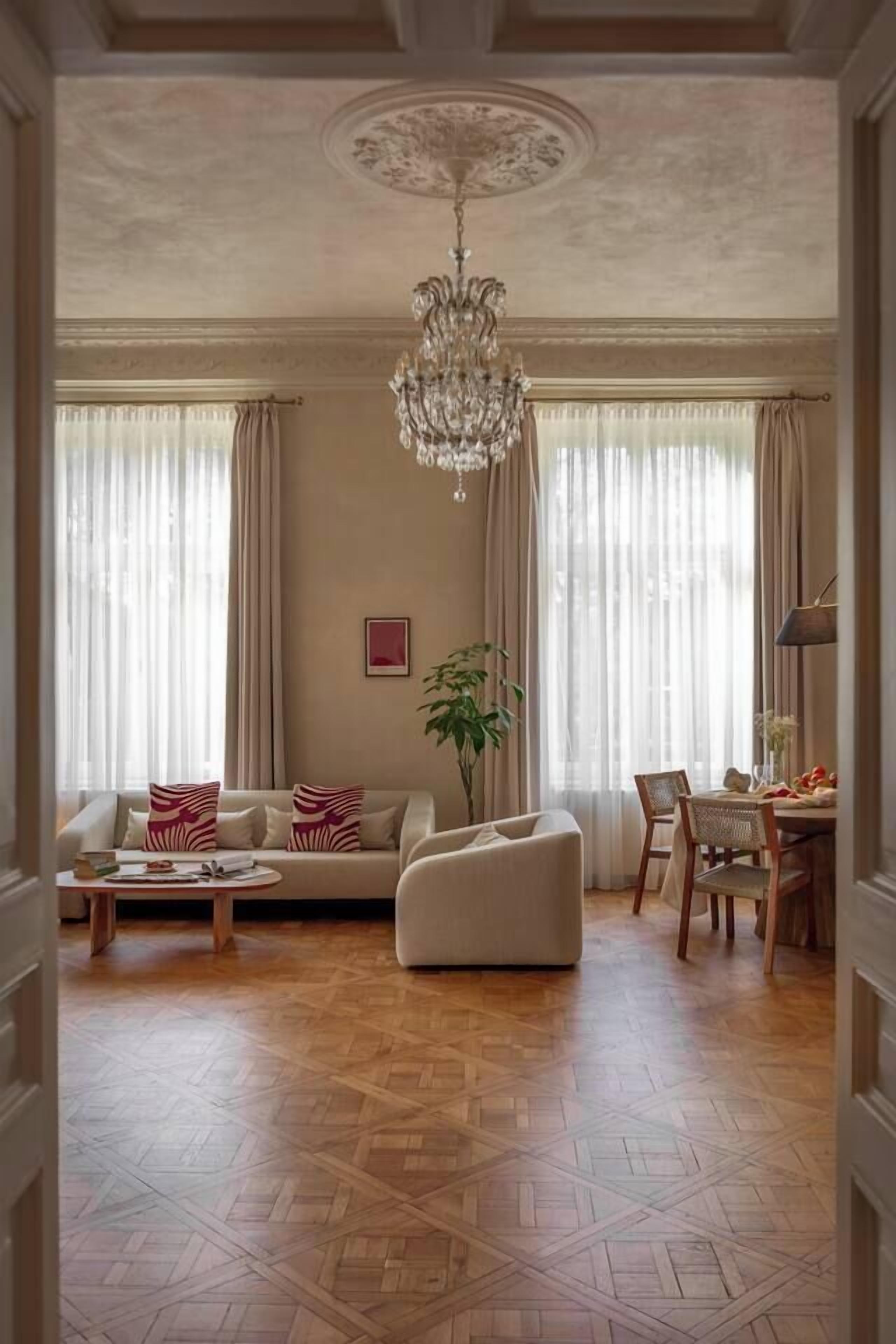 Uma sala de estar ampla, com um candelabro, um sofá, uma mesa de centro e uma área de jantar com cadeiras e uma mesa.